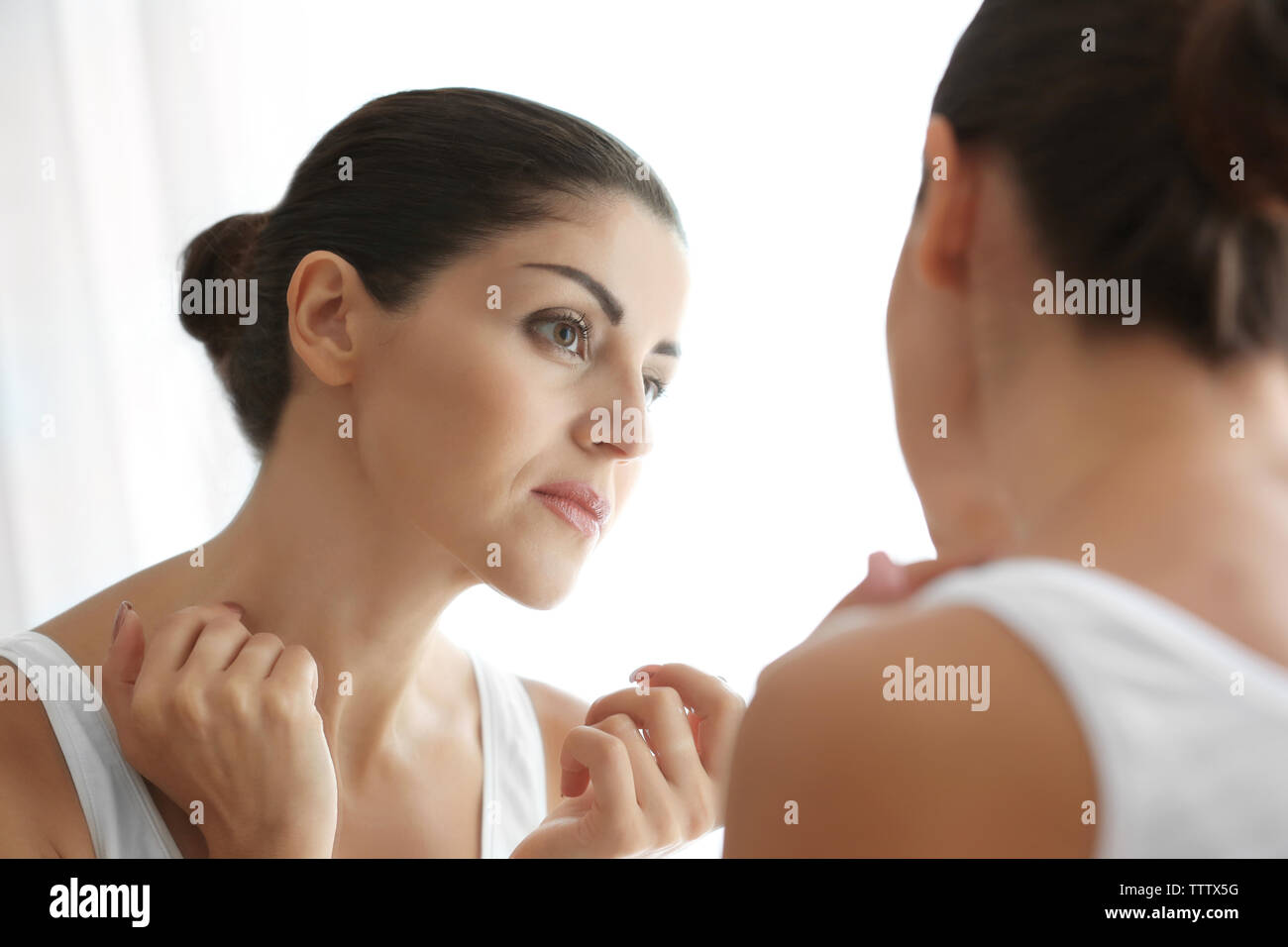Adult woman checking her face in mirror on light background Stock Photo ...