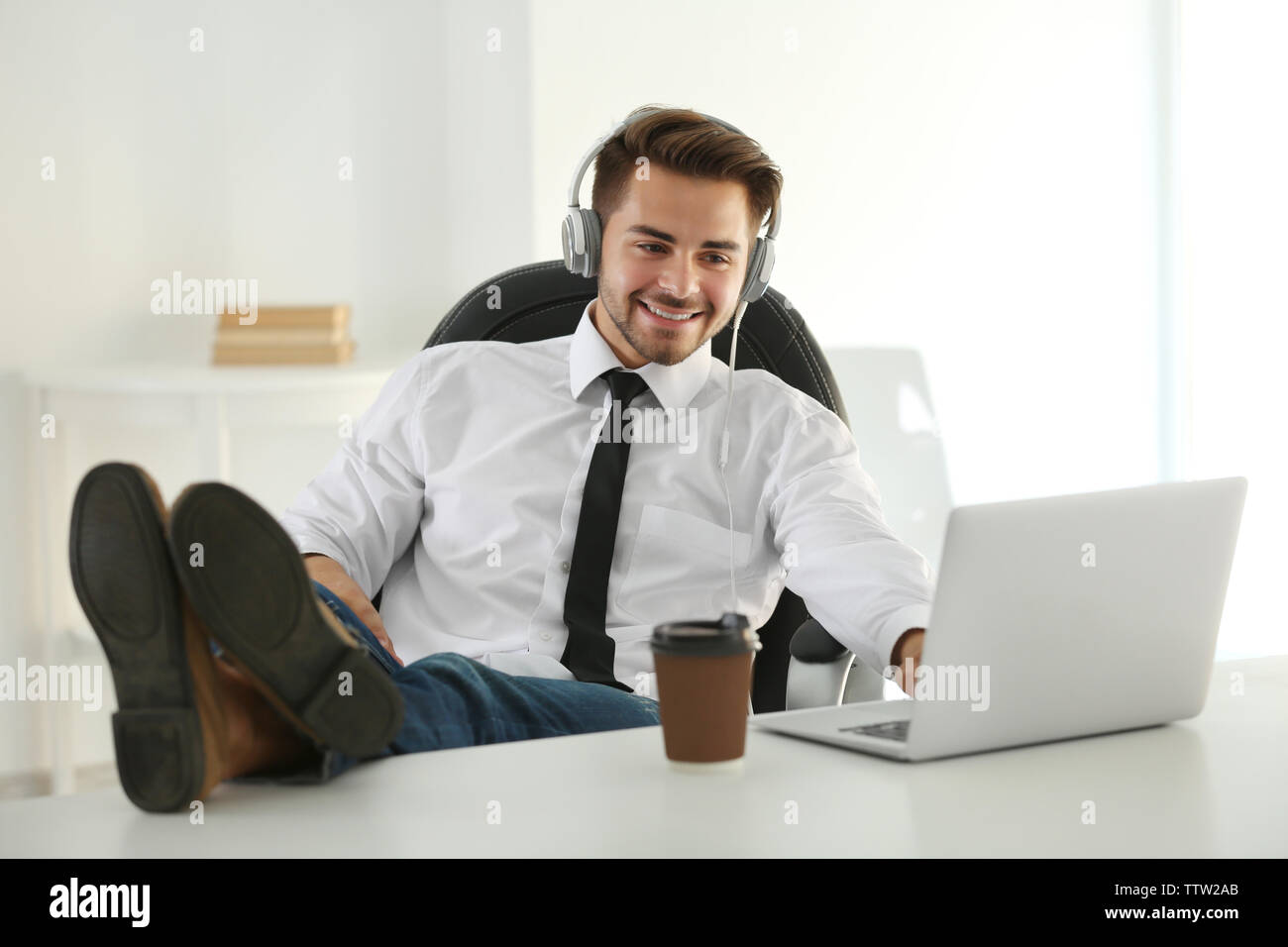 Handsome man listening to music with headphones and putting feet at ...