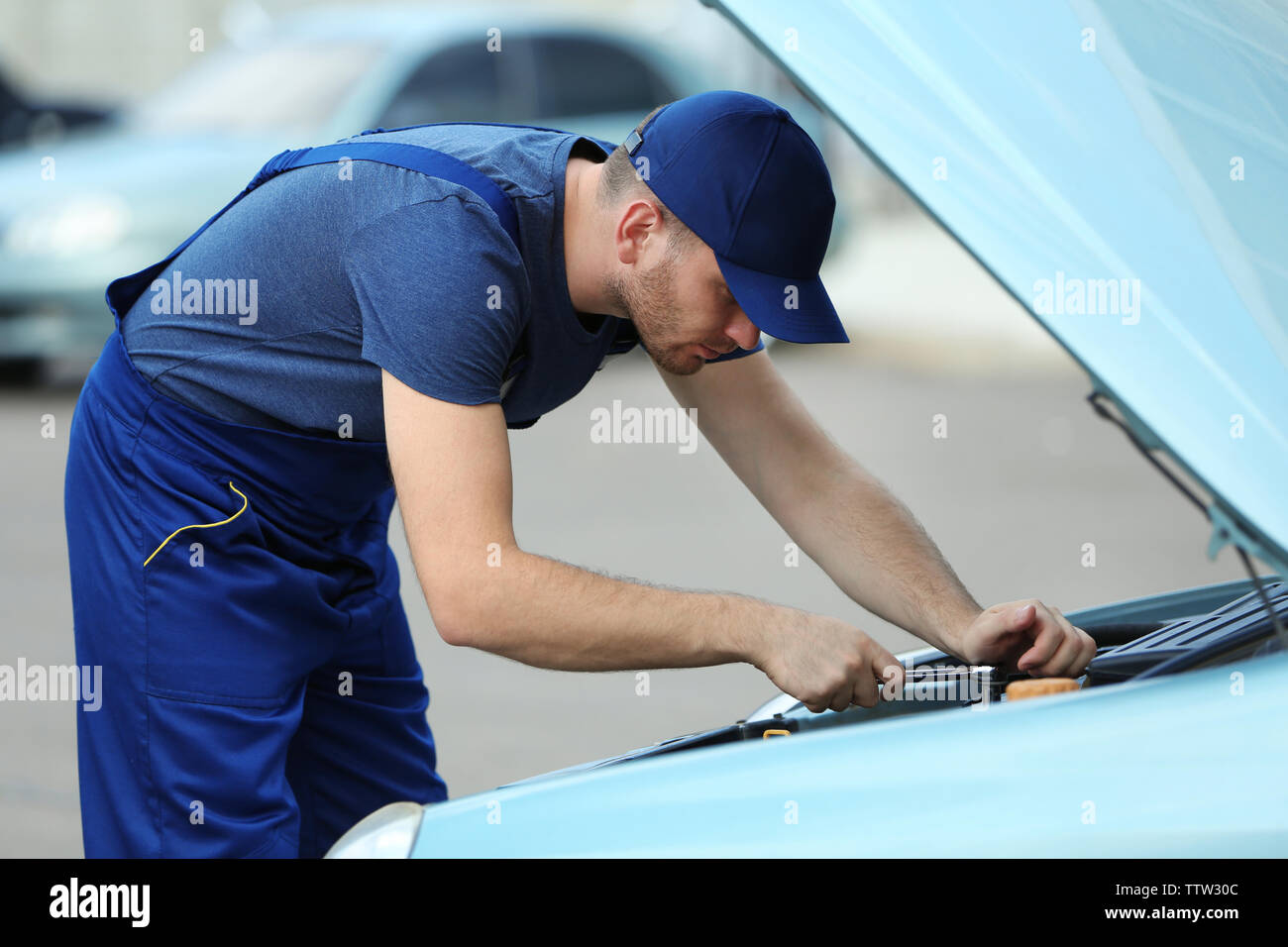 Mechanic standing in front of the open hood and repairing the car Stock ...