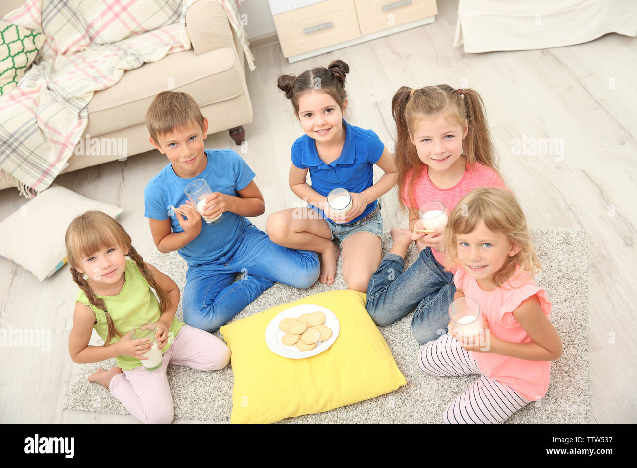 Little children eating cookies and drinking milk while sitting on floor ...