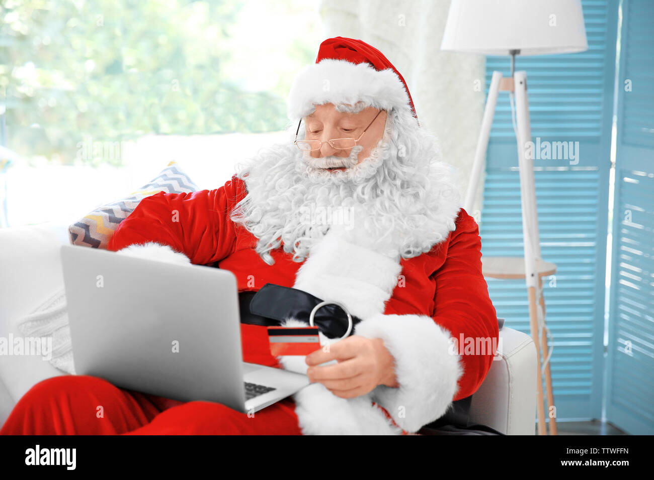Santa Claus with credit card and laptop on couch at home Stock Photo ...