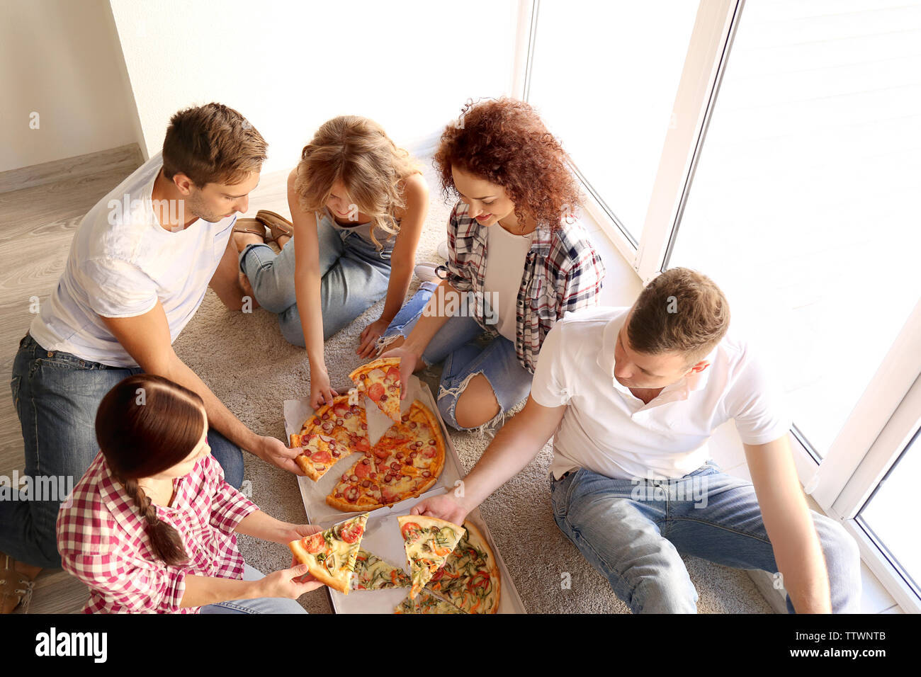 Friends having fun and eating pizza while sitting on floor Stock Photo ...
