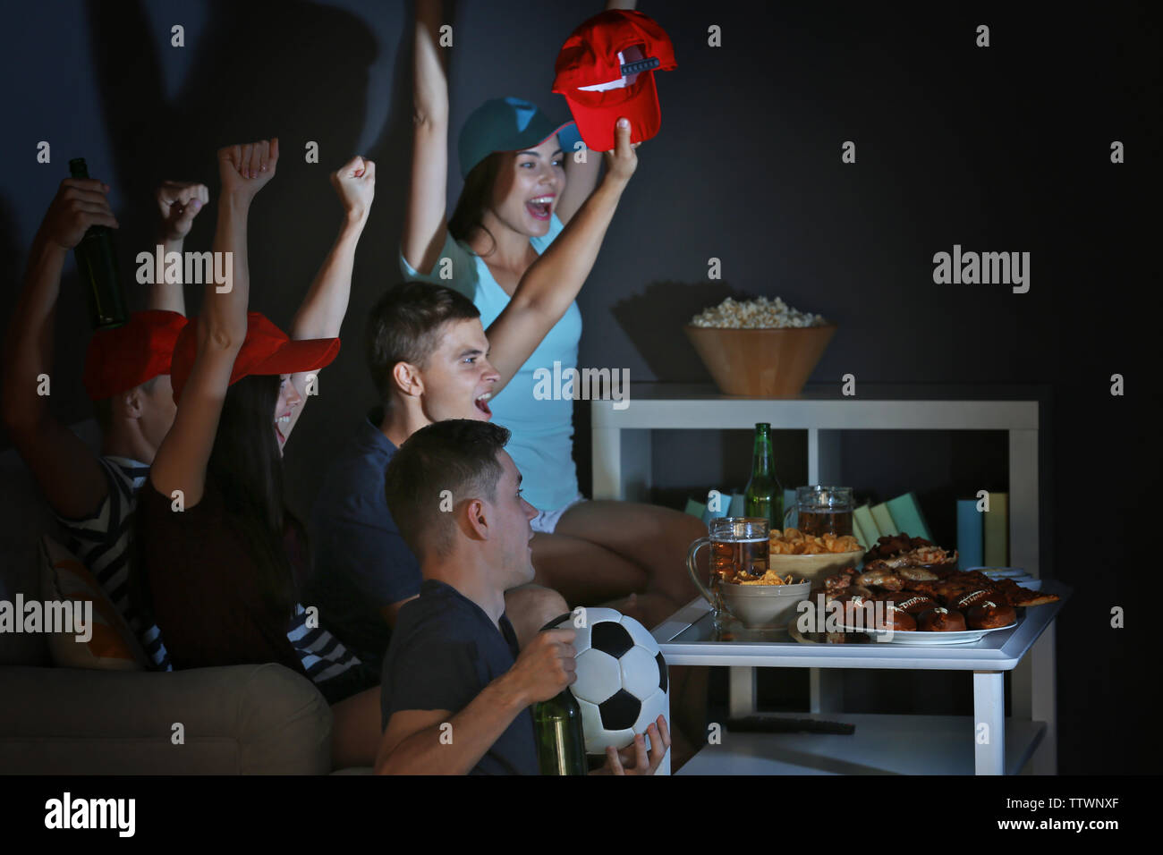 Young fans watching football match on TV late in evening with beer and ...