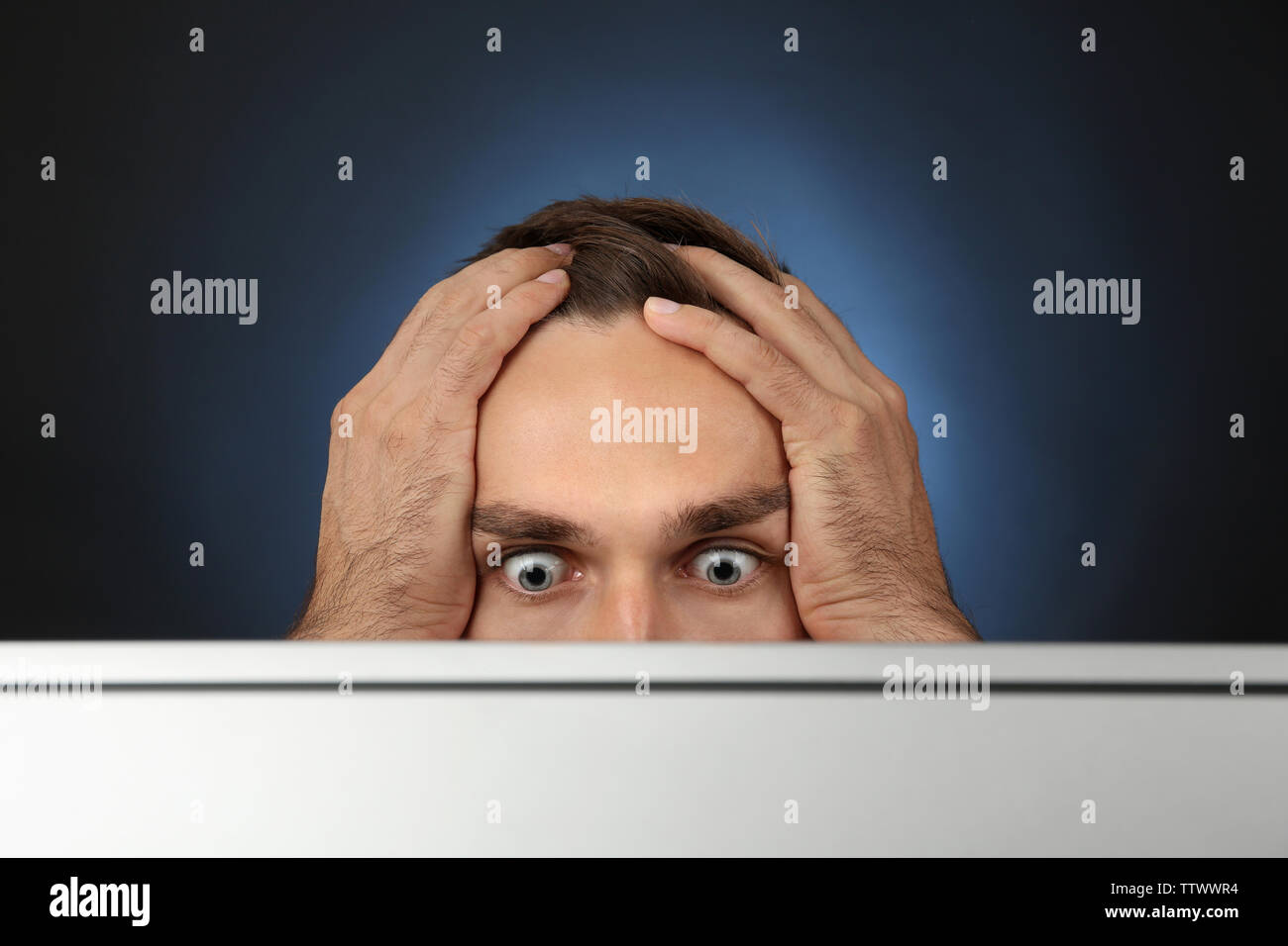 Shocked man sitting at computer monitor on dark background Stock Photo ...