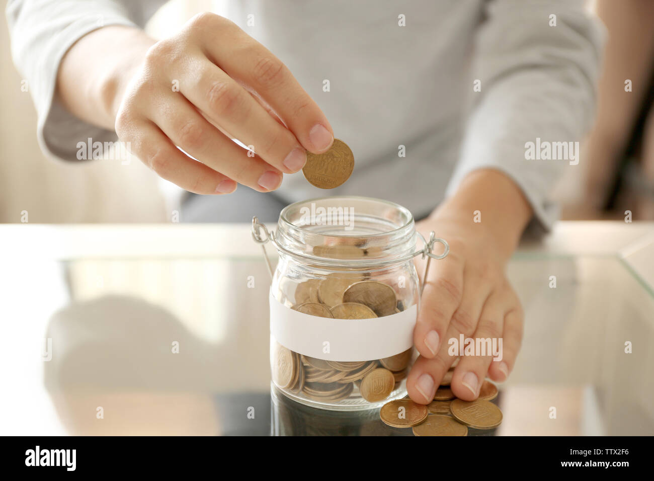 Female hand putting money into glass jar closeup Stock Photo - Alamy