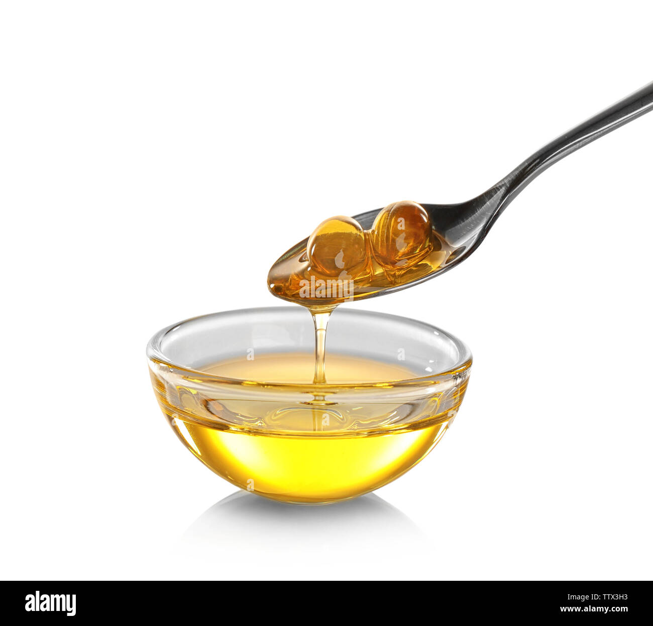 Spoon with gelatin capsules and glass bowl of cod liver oil on white ...