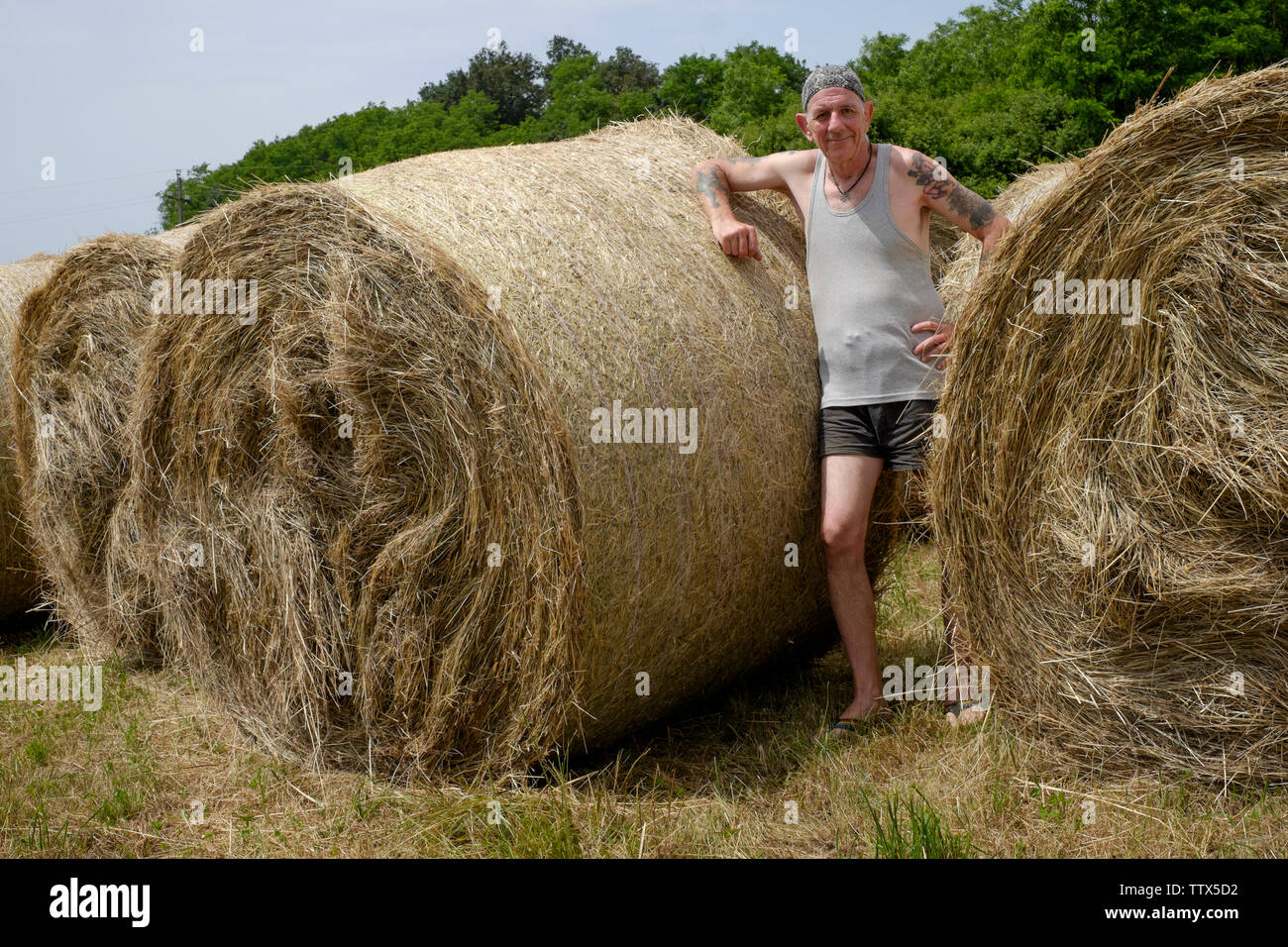 man standing amongst round hay bales while enjoying the hot summer sun ...