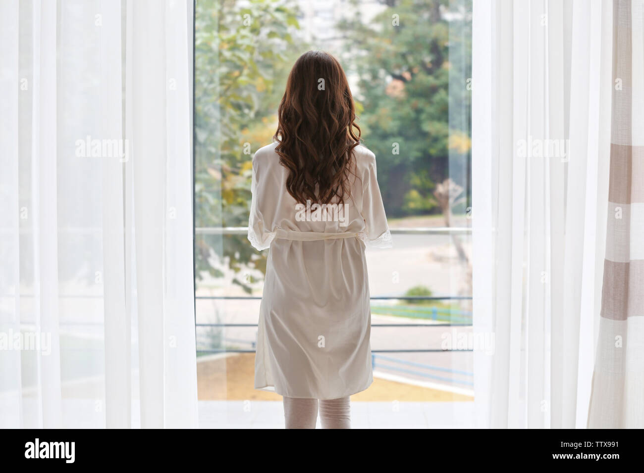 Beautiful woman in white silk robe standing near window Stock Photo - Alamy