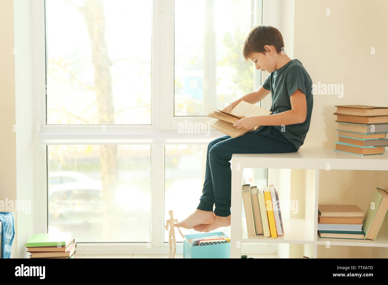 Cute schoolboy sitting beside window and reading book Stock Photo - Alamy