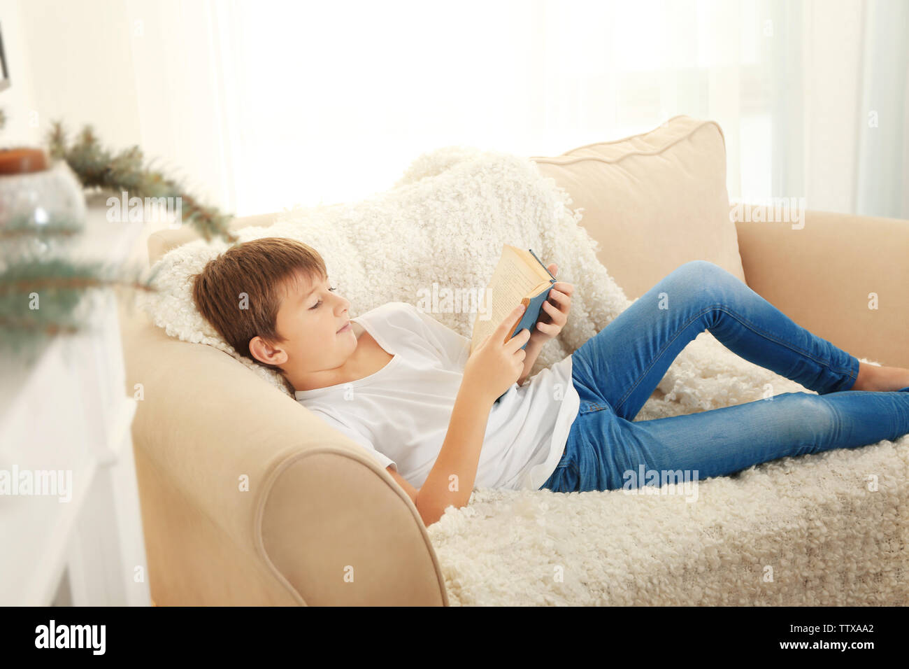 Cute schoolboy reading book on sofa Stock Photo - Alamy