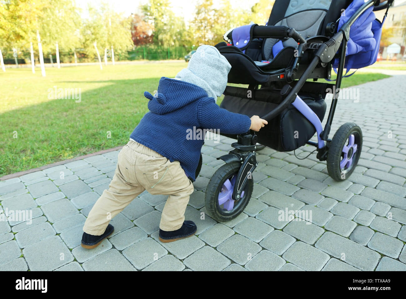 Cute little baby pushing violet stroller outdoors Stock Photo - Alamy