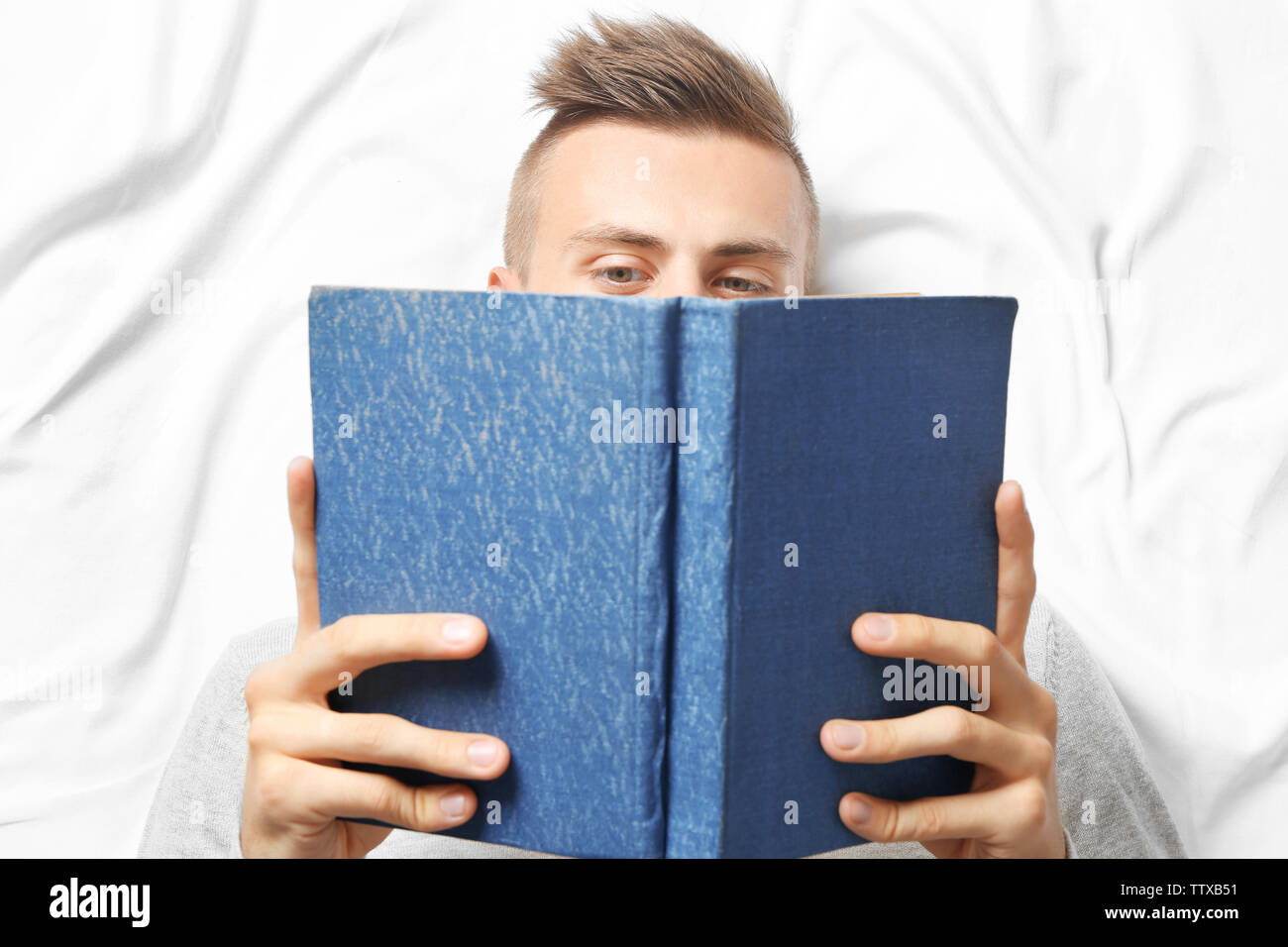 Young man reading book while lying on bed Stock Photo - Alamy