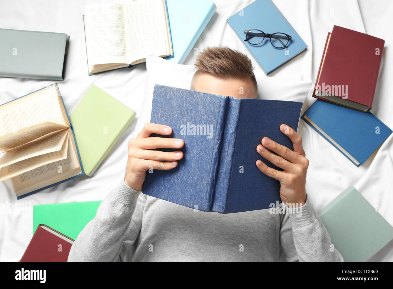 Young man reading book while lying on bed Stock Photo - Alamy