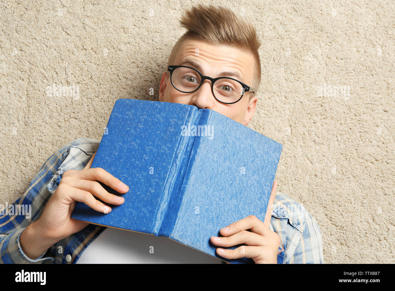 Funny young man with book lying on carpet Stock Photo - Alamy