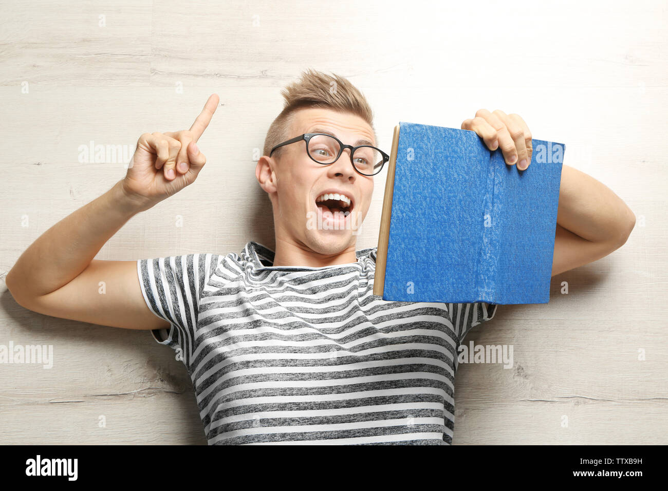 Emotional young man reading book while lying on floor Stock Photo - Alamy