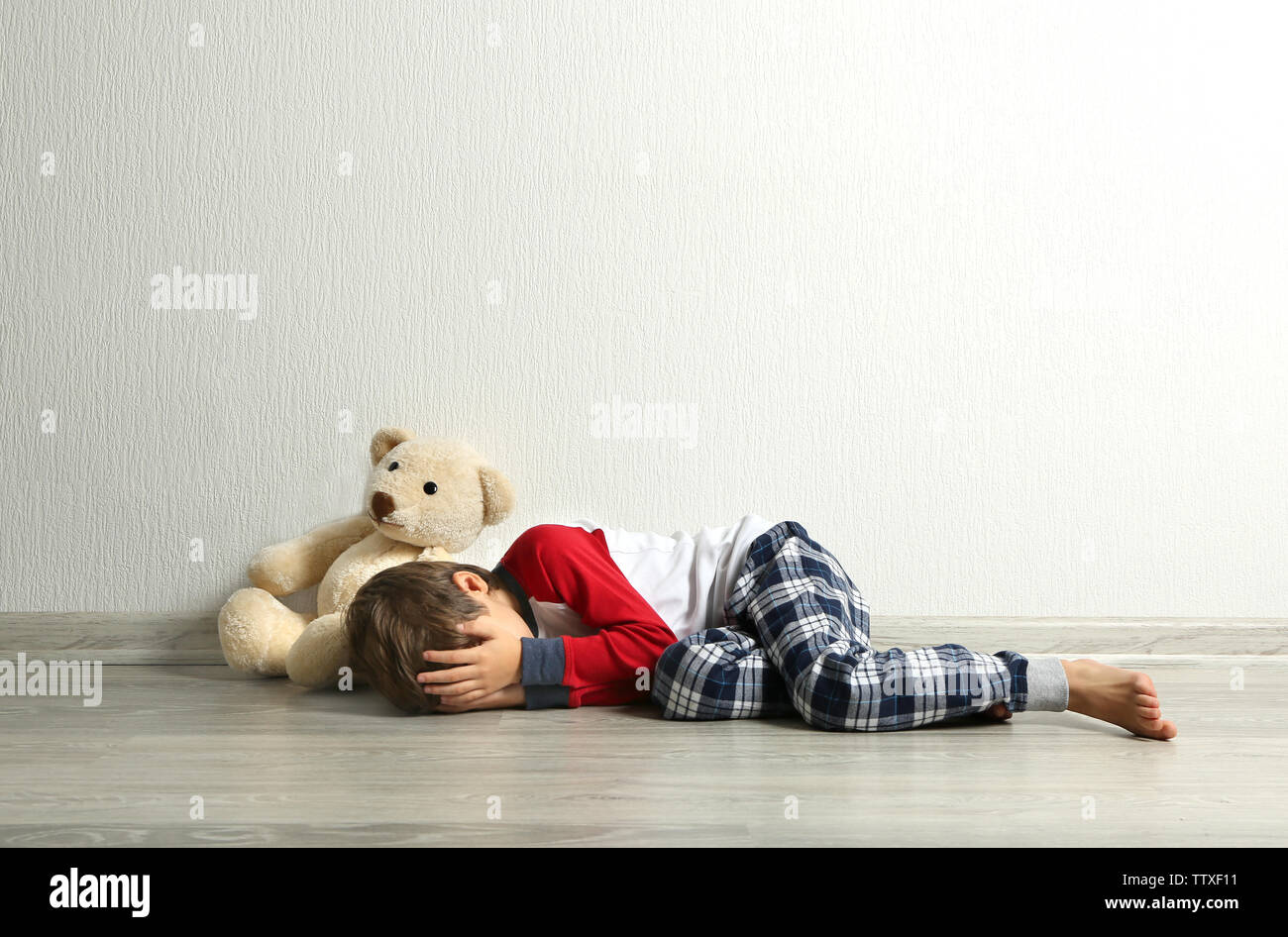 Crying little boy with teddy bear on floor in empty room Stock Photo ...