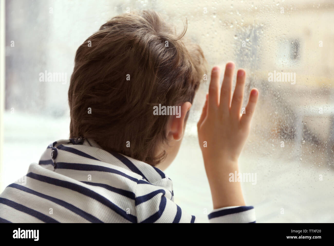 Close up view of little boy looking out of window Stock Photo - Alamy
