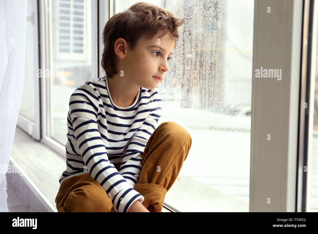 Cute little boy sitting on window sill Stock Photo - Alamy
