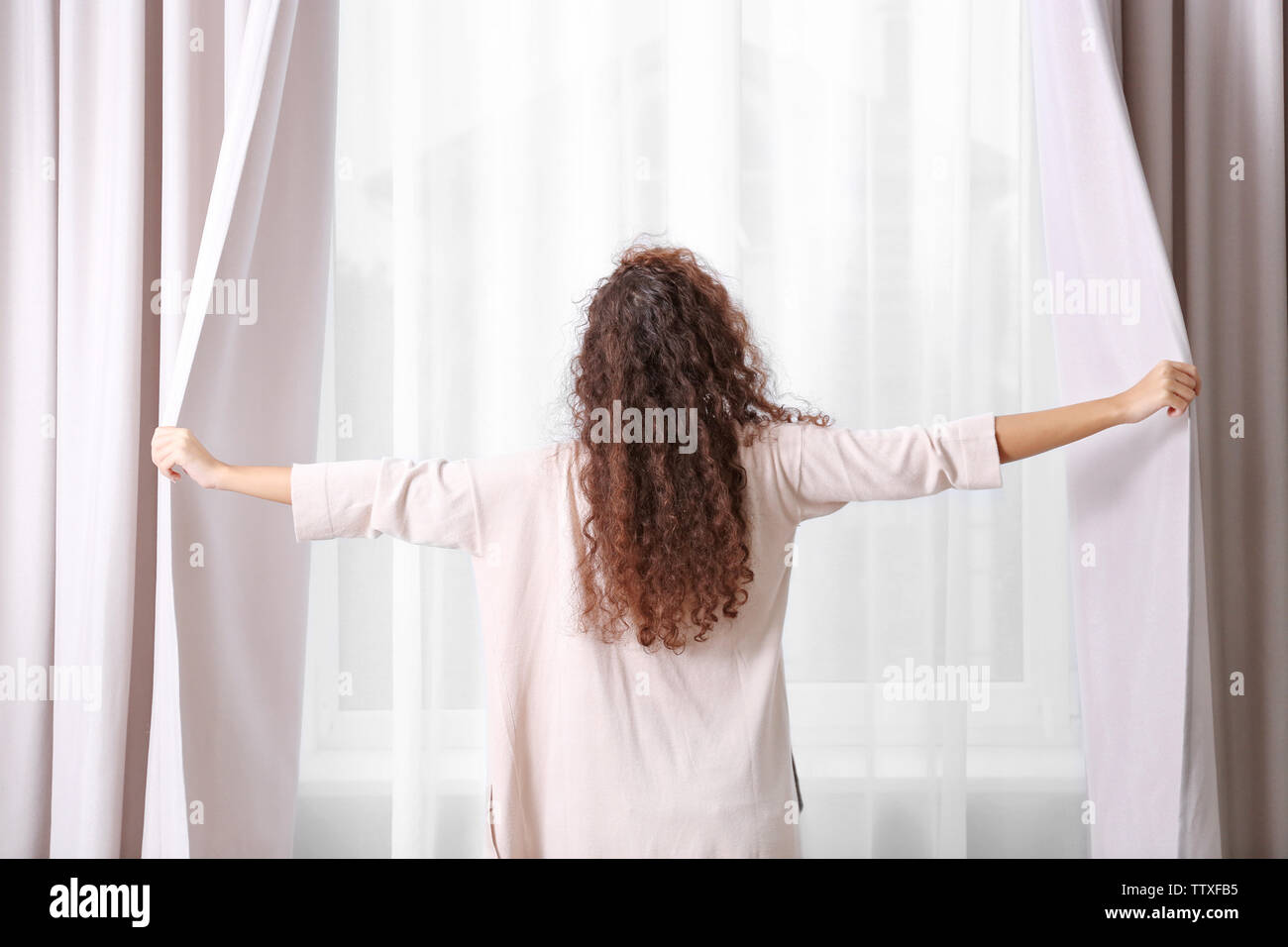 Woman opening curtains in room Stock Photo - Alamy