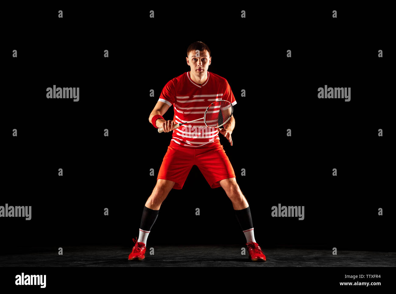 Young man playing badminton isolated on black background in mixed light ...