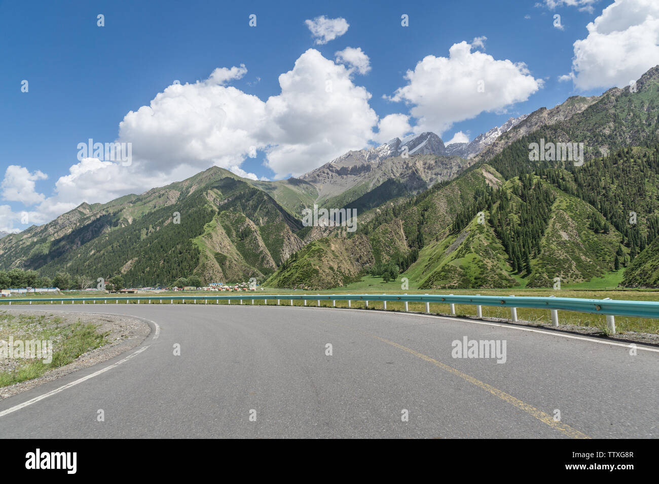 G217 Duku Highway bend in alpine forest under summer blue sky and white ...