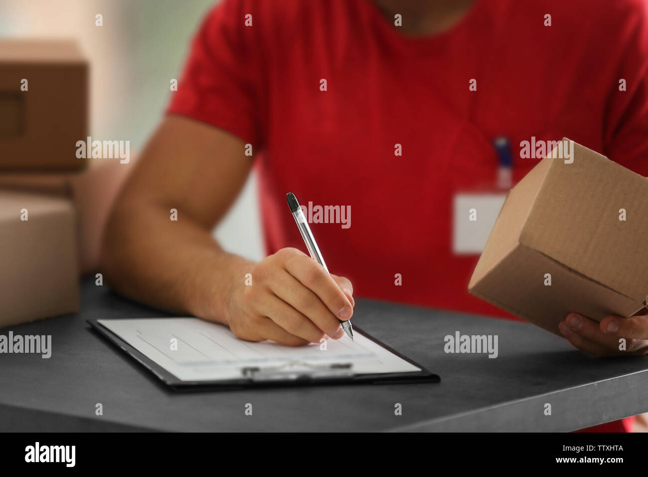 Courier making notes in delivery receipt at table Stock Photo - Alamy