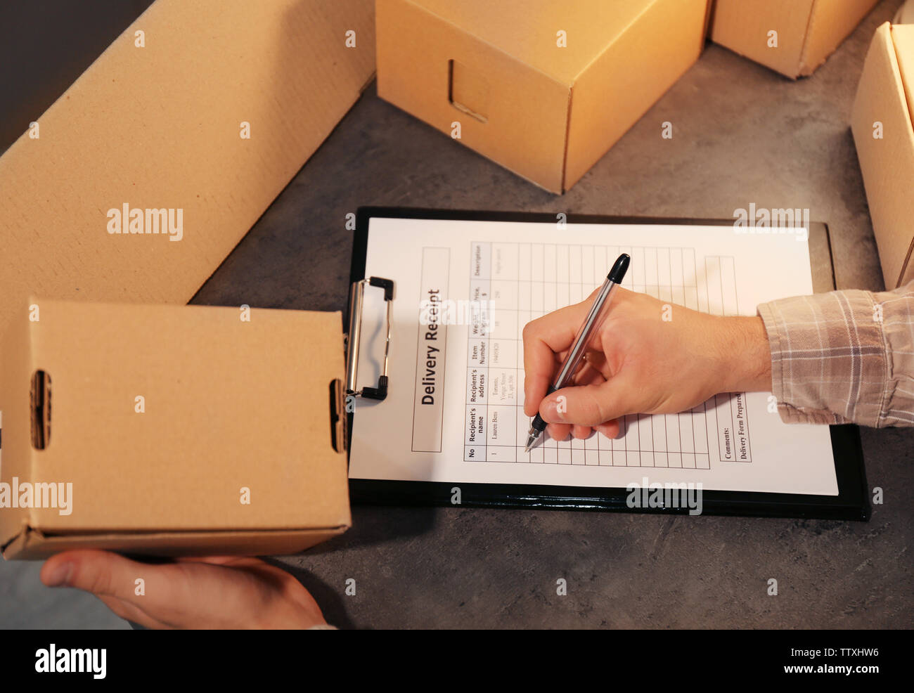 Courier making notes in delivery receipt at table Stock Photo - Alamy