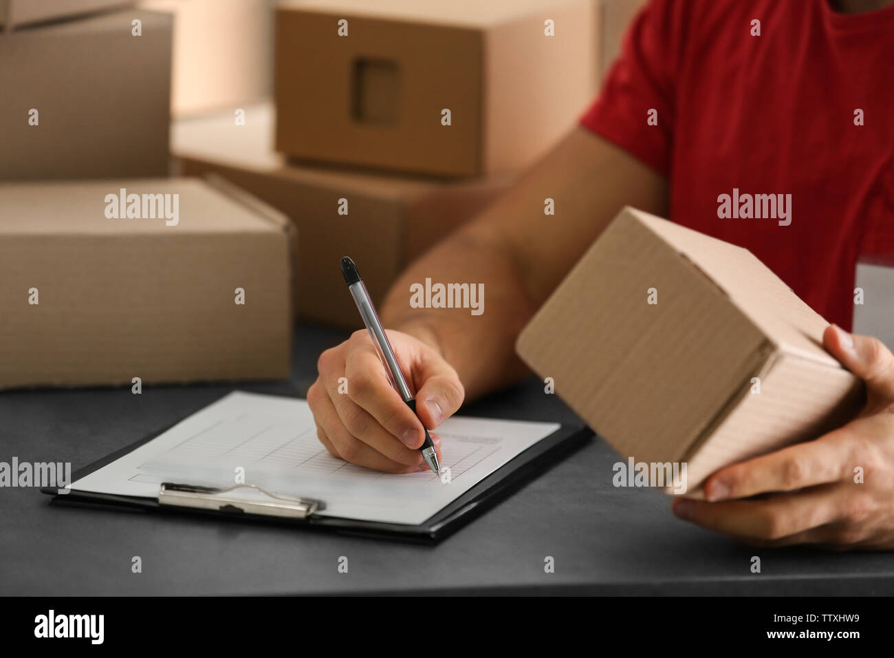Courier making notes in delivery receipt at table Stock Photo - Alamy