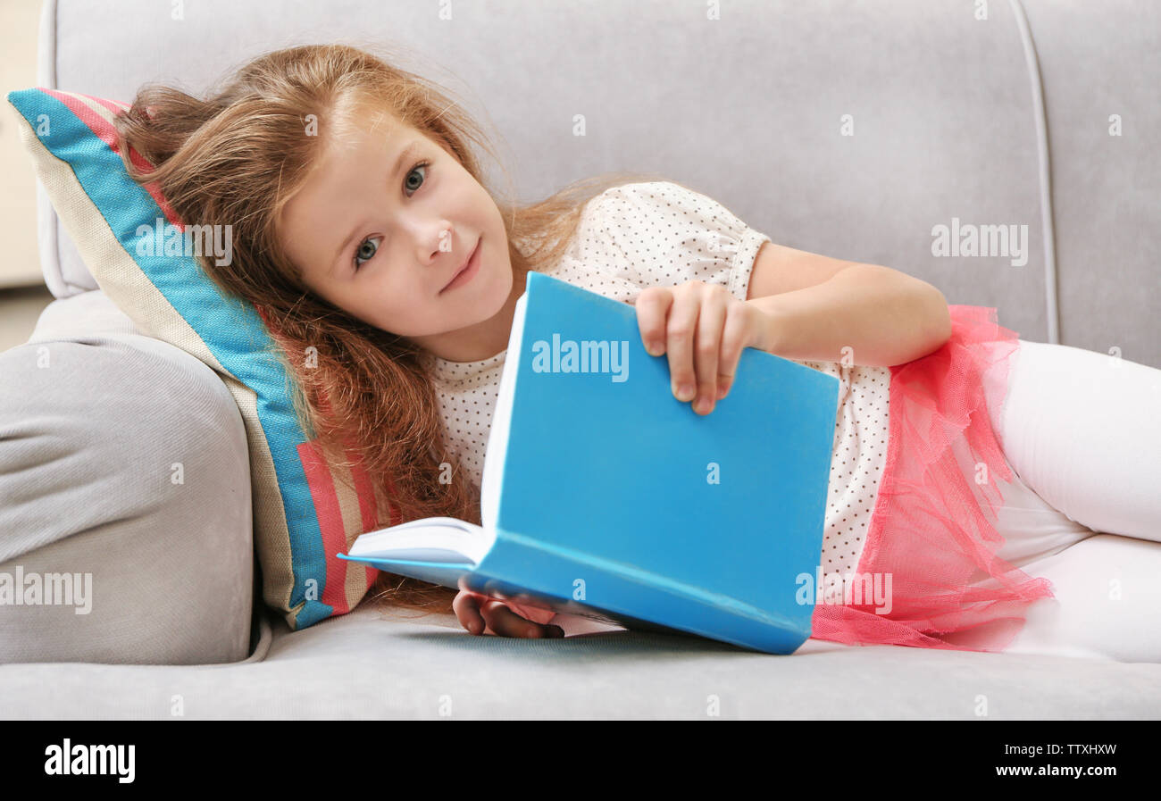 Cute girl reading book on couch Stock Photo - Alamy