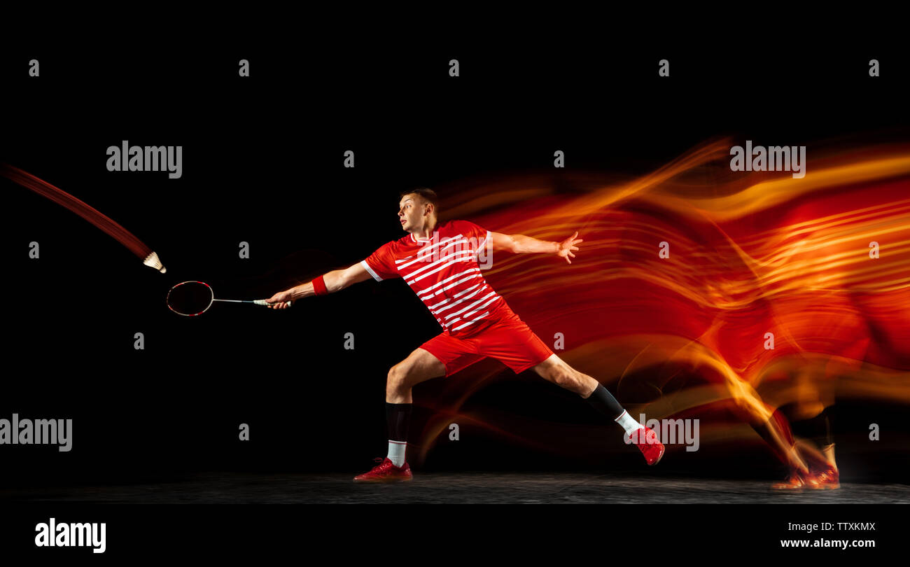 Young man playing badminton isolated on black background in mixed light ...