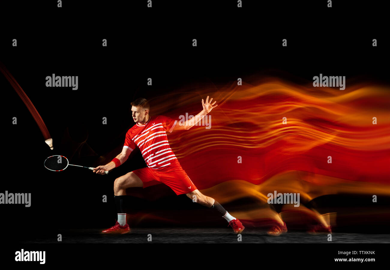 Young man playing badminton isolated on black background in mixed light ...