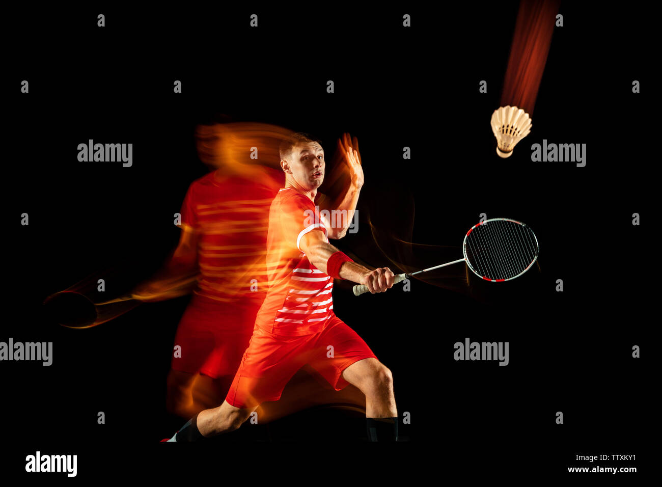 Young man playing badminton isolated on black background in mixed light ...