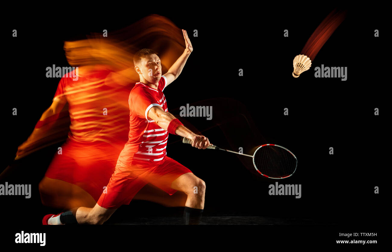Young man playing badminton isolated on black background in mixed light ...