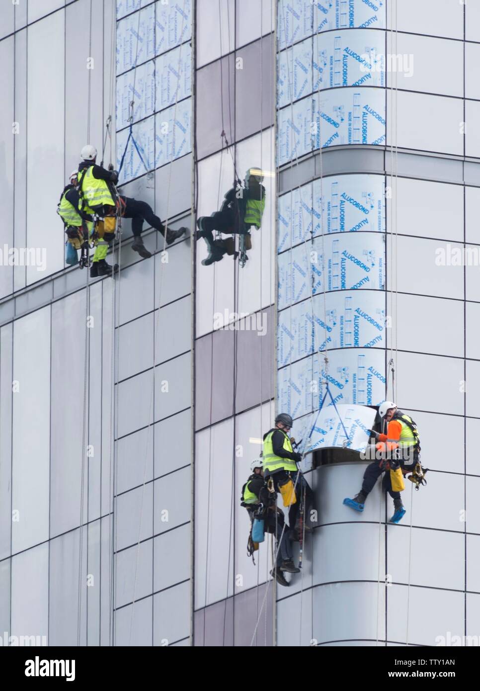 Workers use abseiling equipment to replace exterior unsafe cladding ...