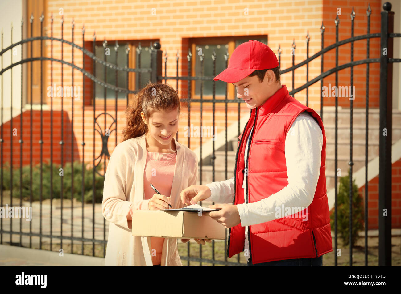 Young woman signing receipt for delivering parcel from male courier ...