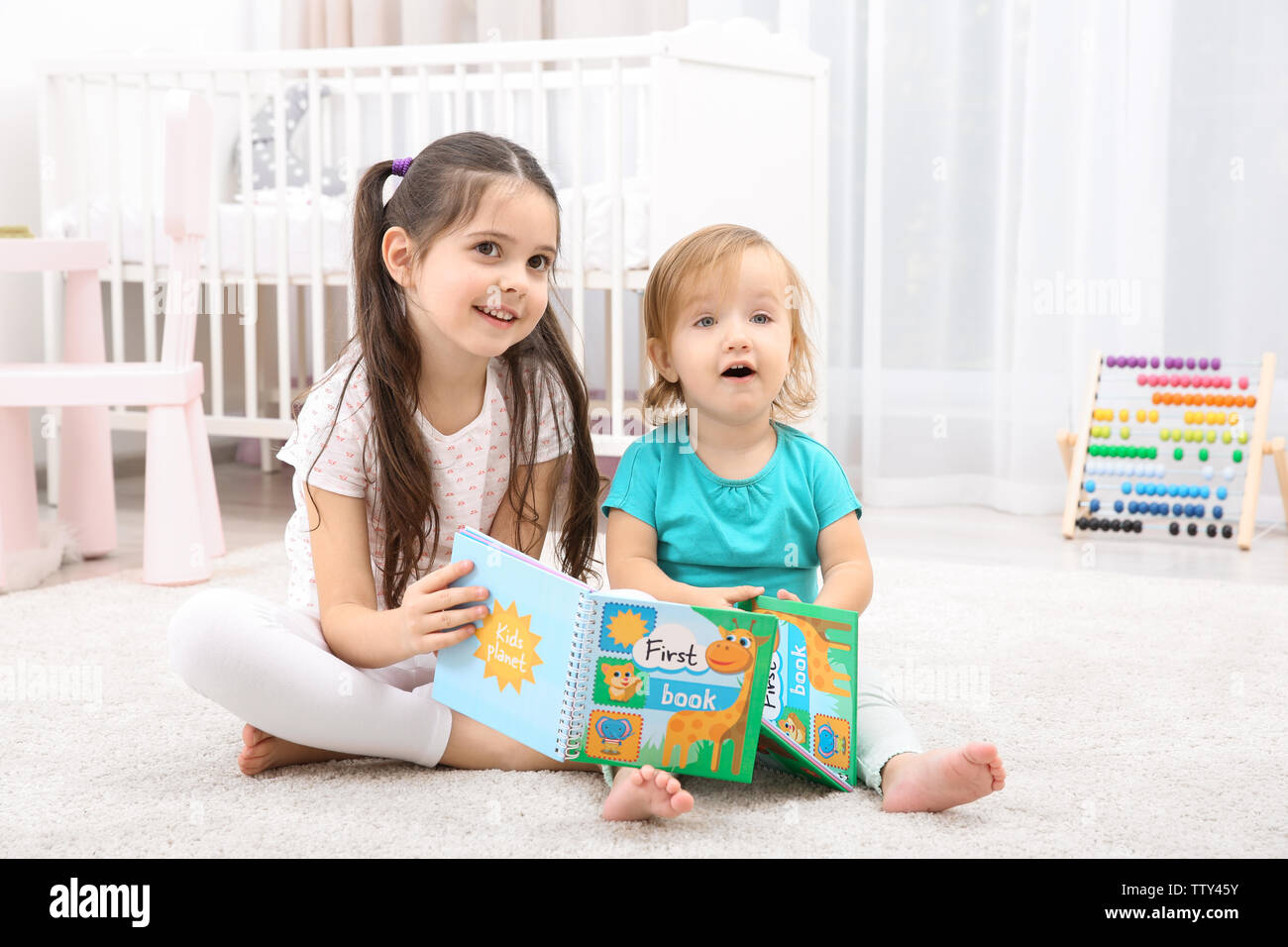 Cute girl reading book with little sister at home Stock Photo - Alamy