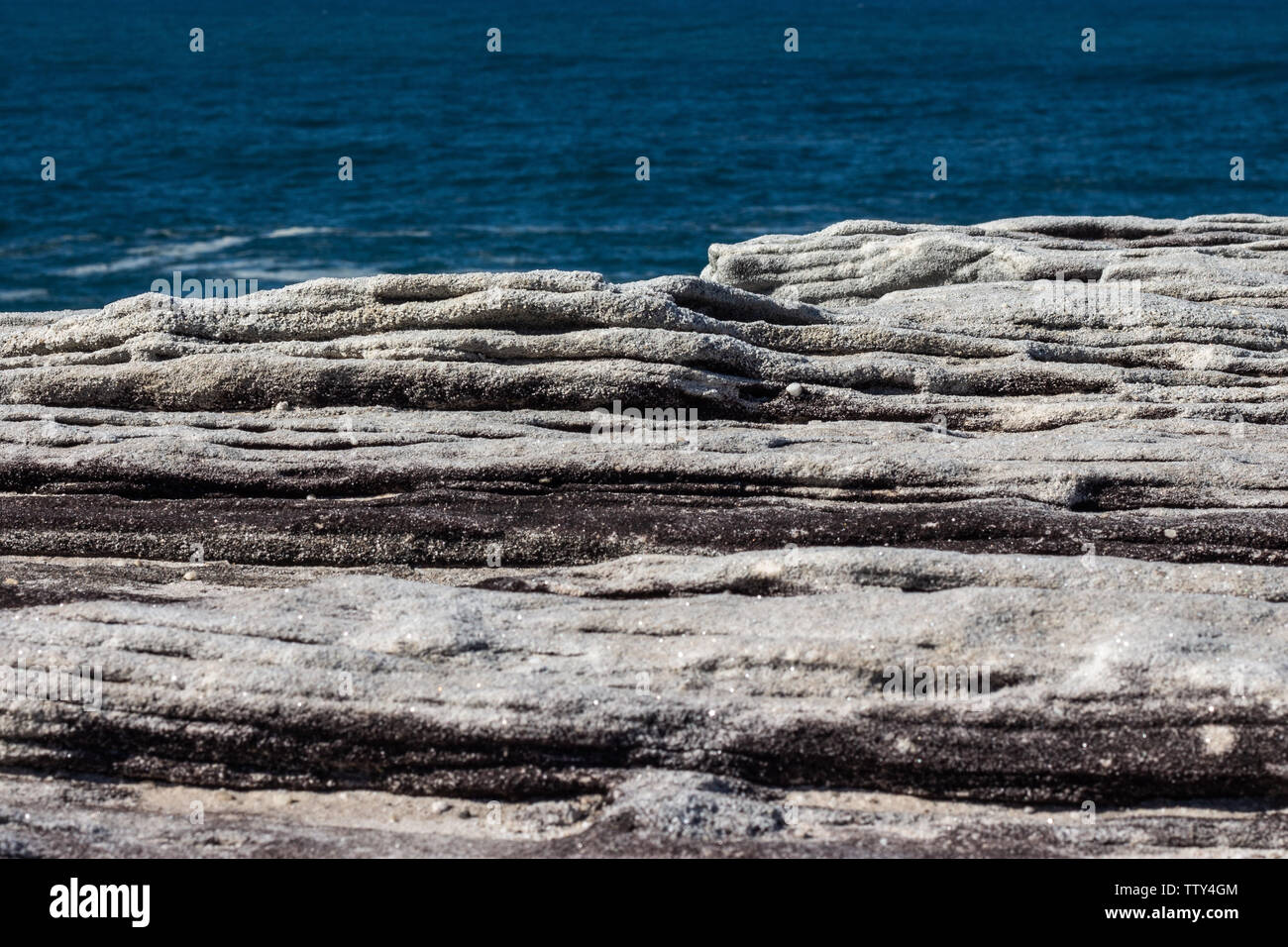 Oceanside rocky cliff top sandstone wave ridges with blue coastal sea ...