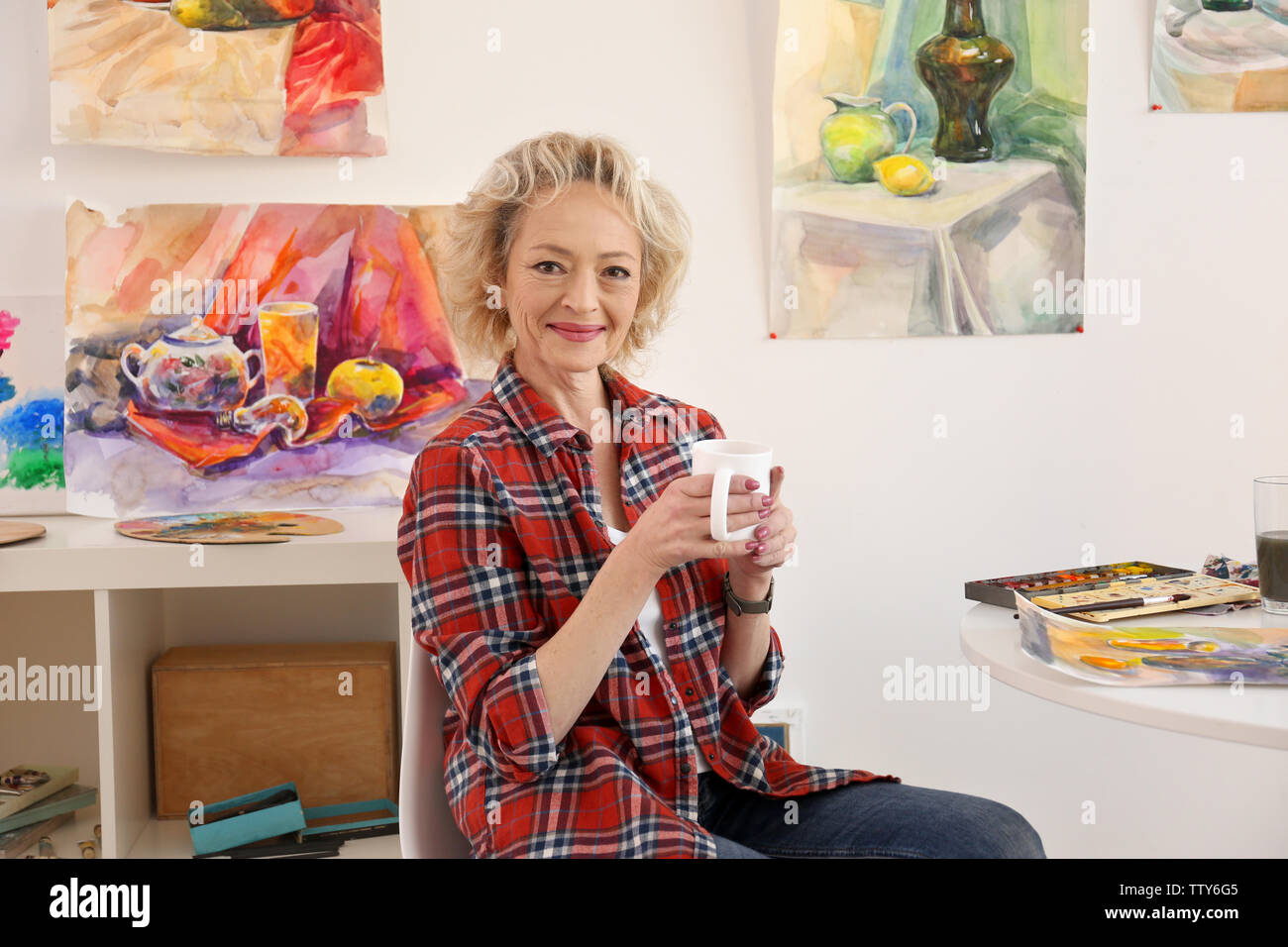Senior female artist drinking coffee in studio Stock Photo - Alamy