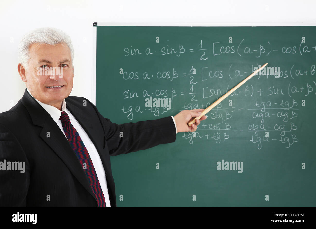Senior teacher with pointer explaining lesson beside blackboard on ...