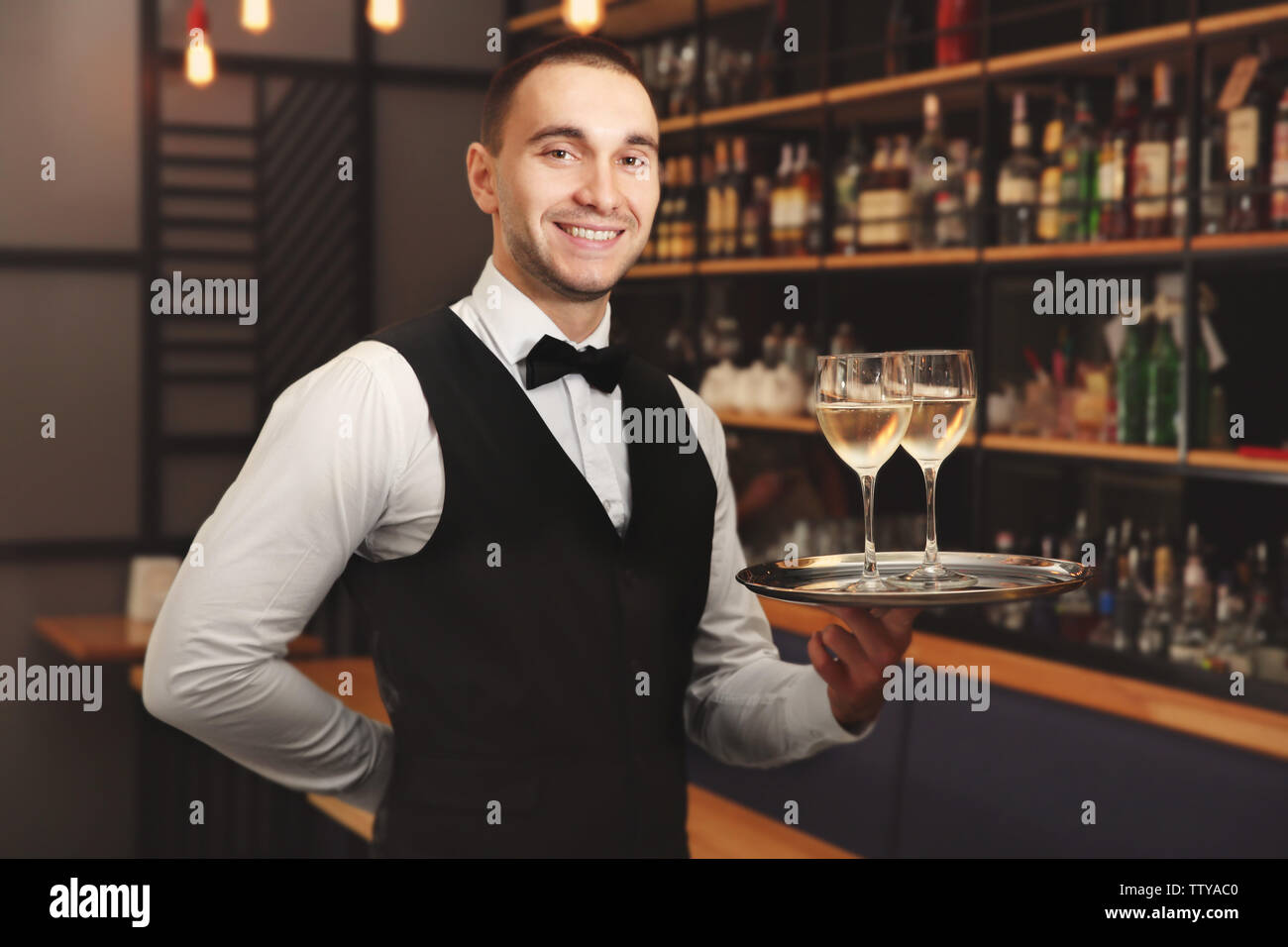 Young handsome waiter holding tray with wine glasses in the restaurant ...