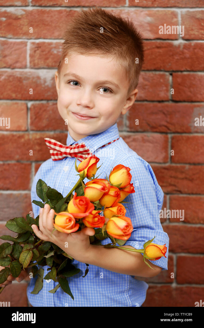 Cute boy with bouquet of beautiful flowers near brick wall Stock Photo ...
