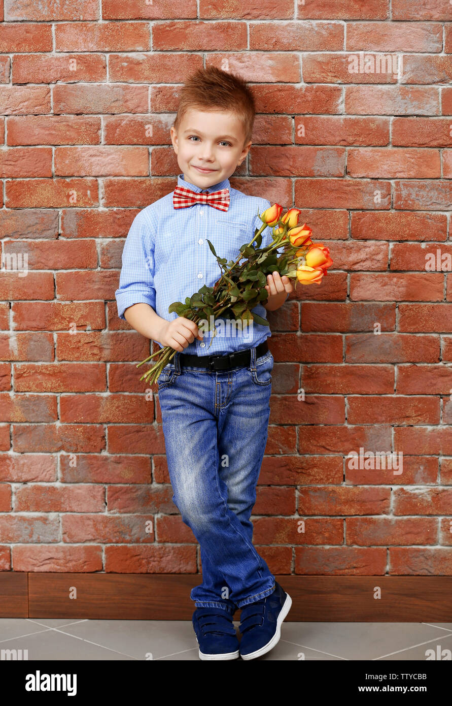 Cute boy with bouquet of beautiful flowers near brick wall Stock Photo ...