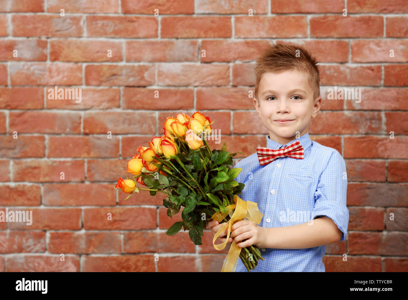Cute boy with bouquet of beautiful flowers near brick wall Stock Photo ...