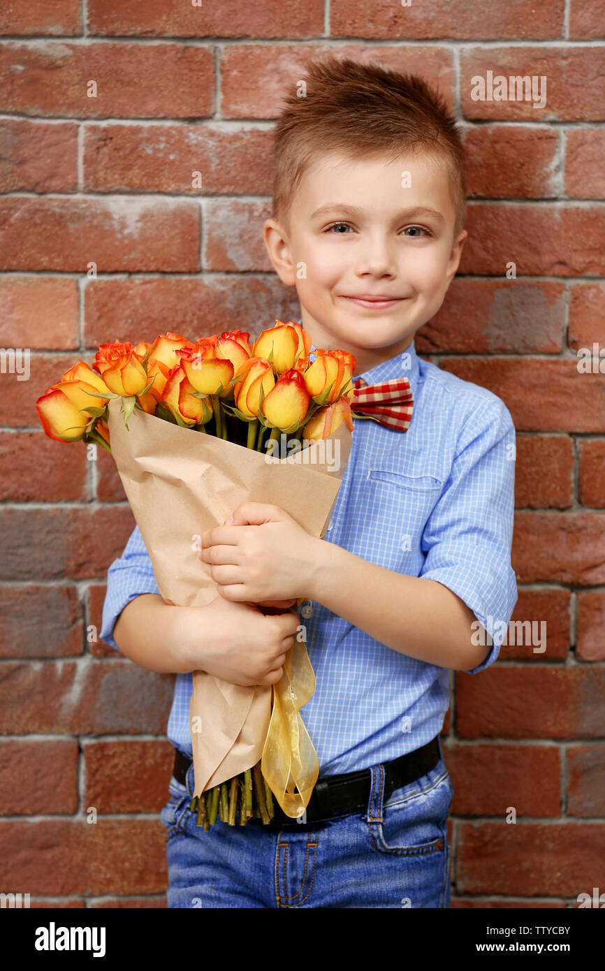 Cute boy with bouquet of beautiful flowers near brick wall Stock Photo ...