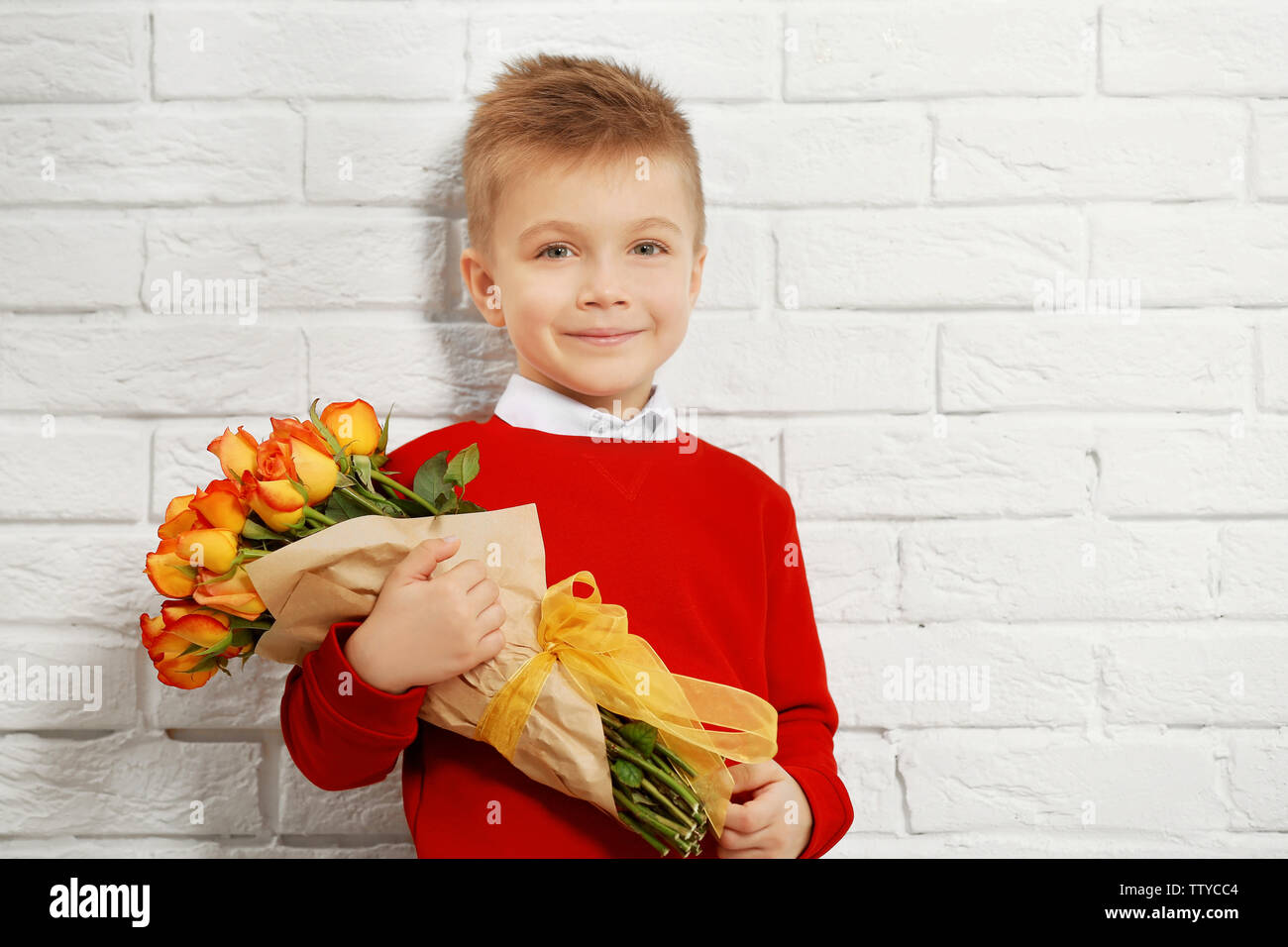 Cute boy with bouquet of beautiful flowers near light brick wall Stock ...