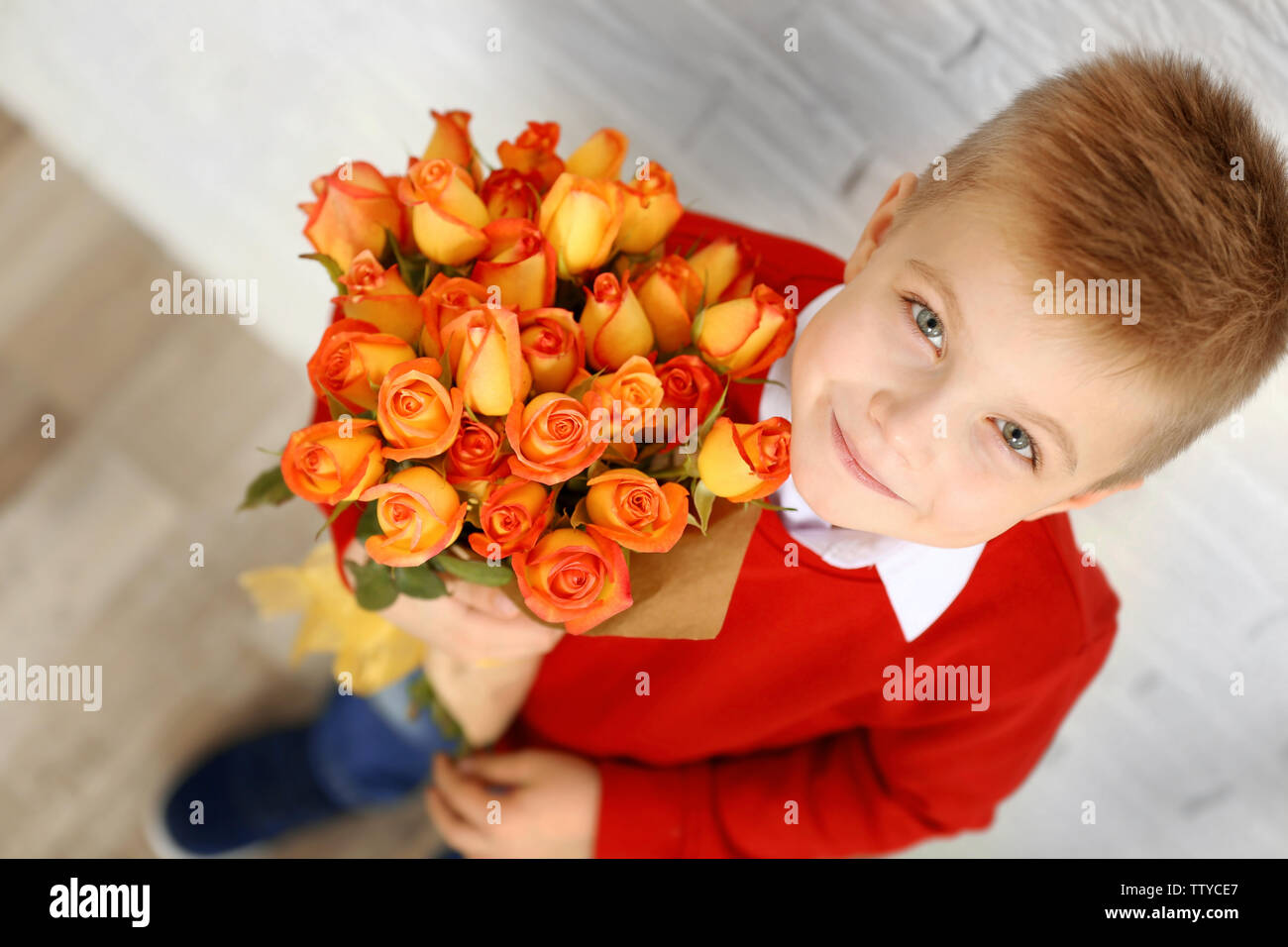 Cute boy with bouquet of beautiful flowers near light brick wall Stock ...