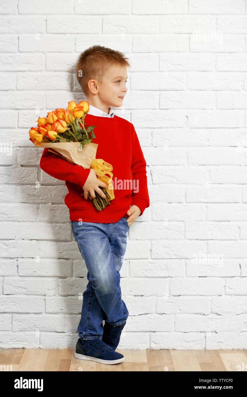 Cute boy with bouquet of beautiful flowers near light brick wall Stock ...