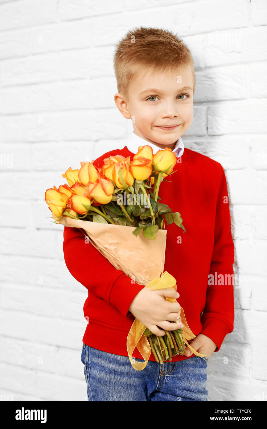Cute boy with bouquet of beautiful flowers near light brick wall Stock ...