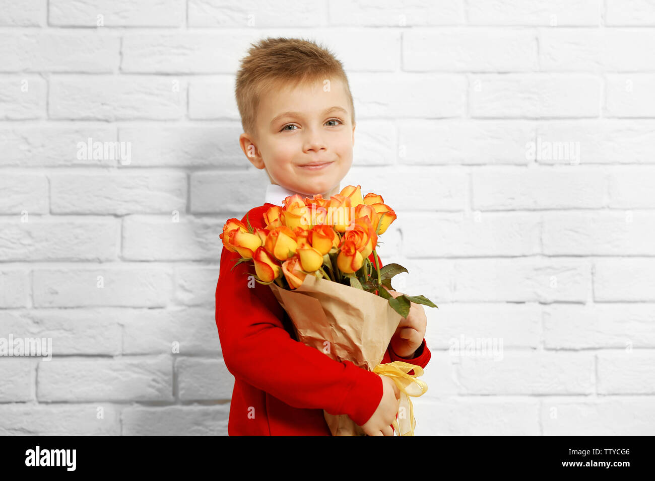 Cute boy with bouquet of beautiful flowers near light brick wall Stock ...