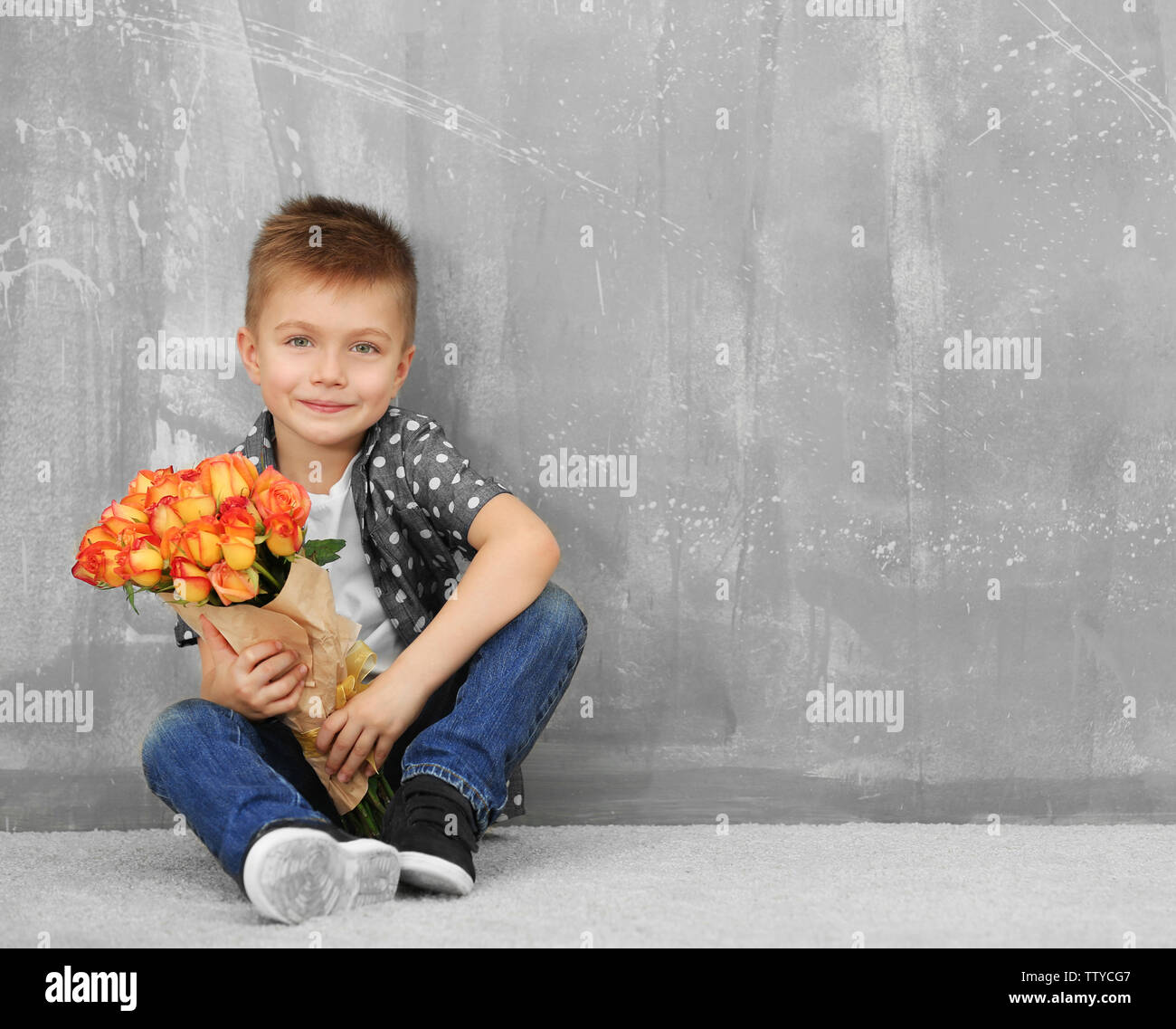 Cute boy with bouquet of beautiful flowers sitting on floor near grunge ...